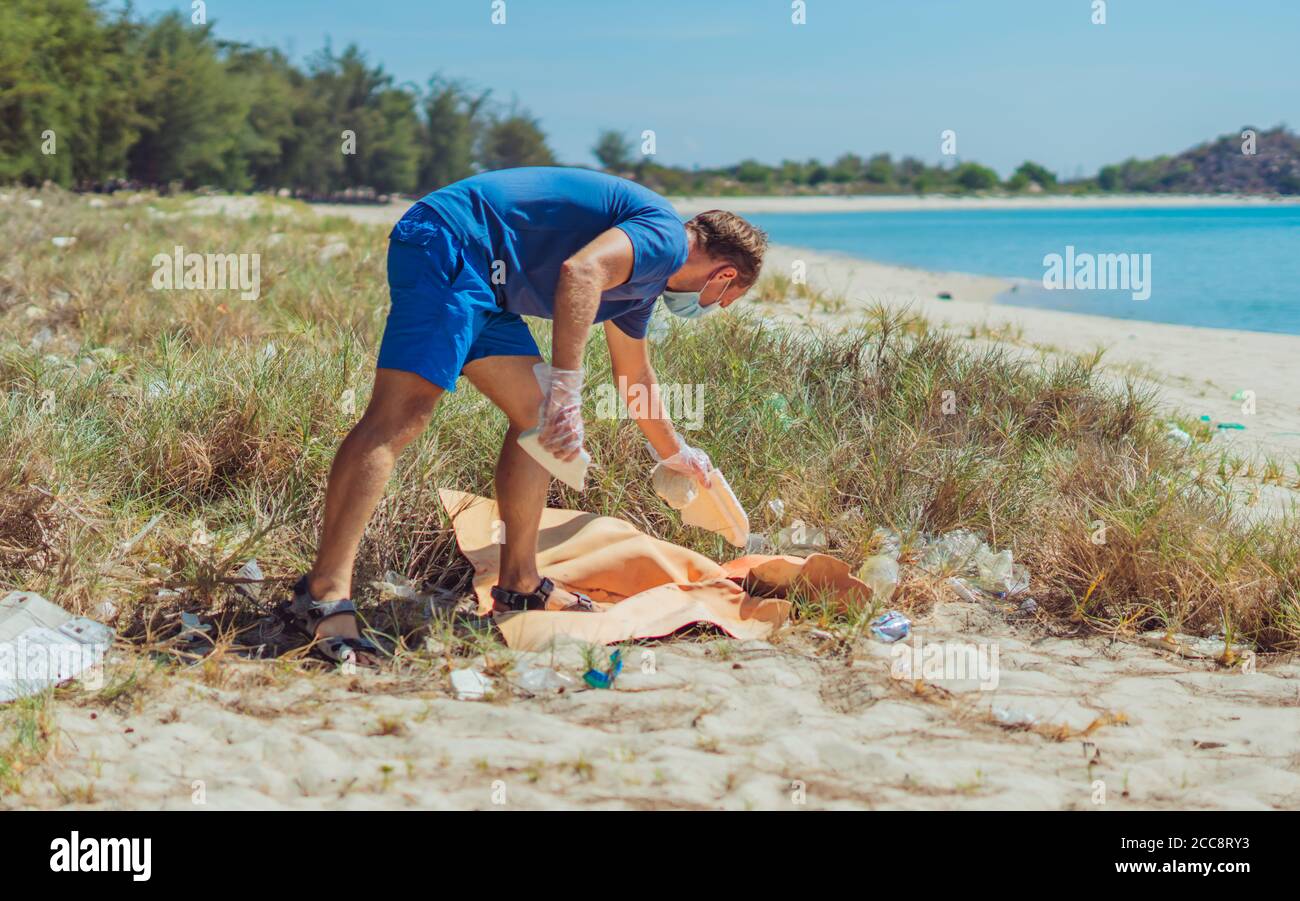 Volunteer in blue face mask lazur sea sand beach. Active man pick up ...