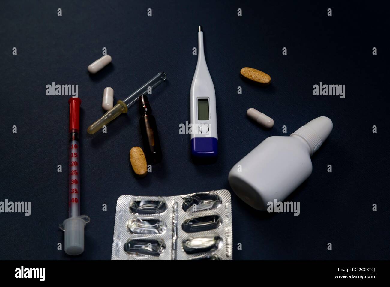 Cold medicines, pills, drops, pipette, thermometer on a solid black ...
