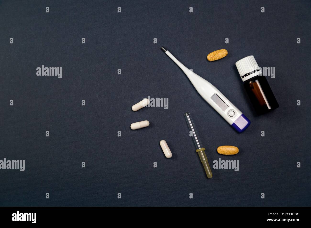 Cold medicines, pills, drops, pipette, thermometer on a black paper ...