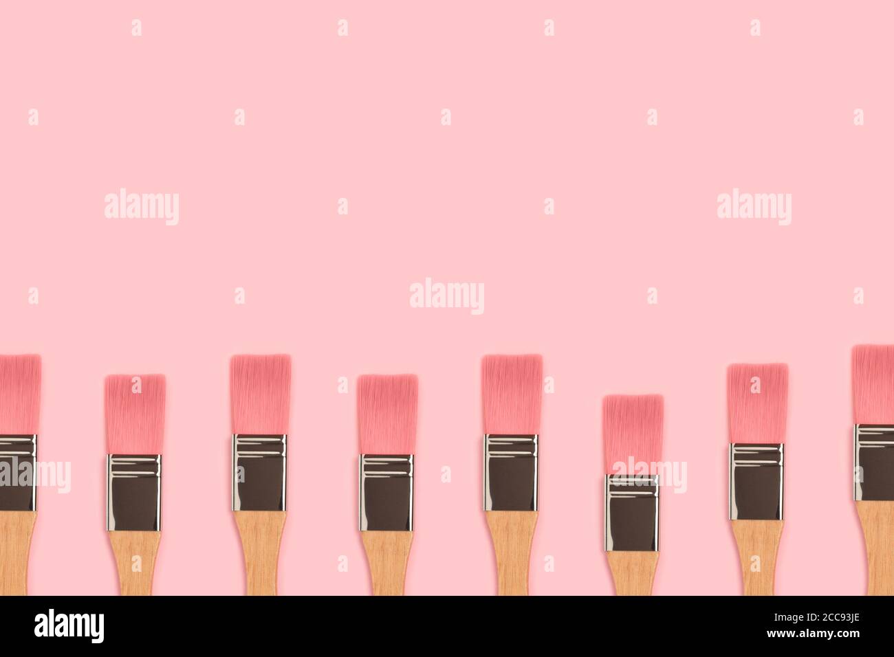 Row of paint brushes on a pink pastel background. Border frame with ...
