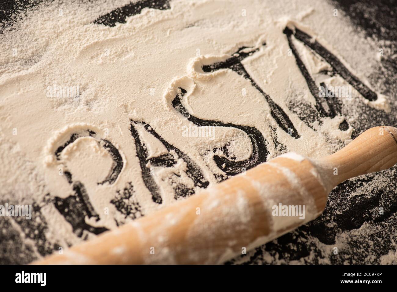 pasta lettering written on flour near rolling pin on black background ...