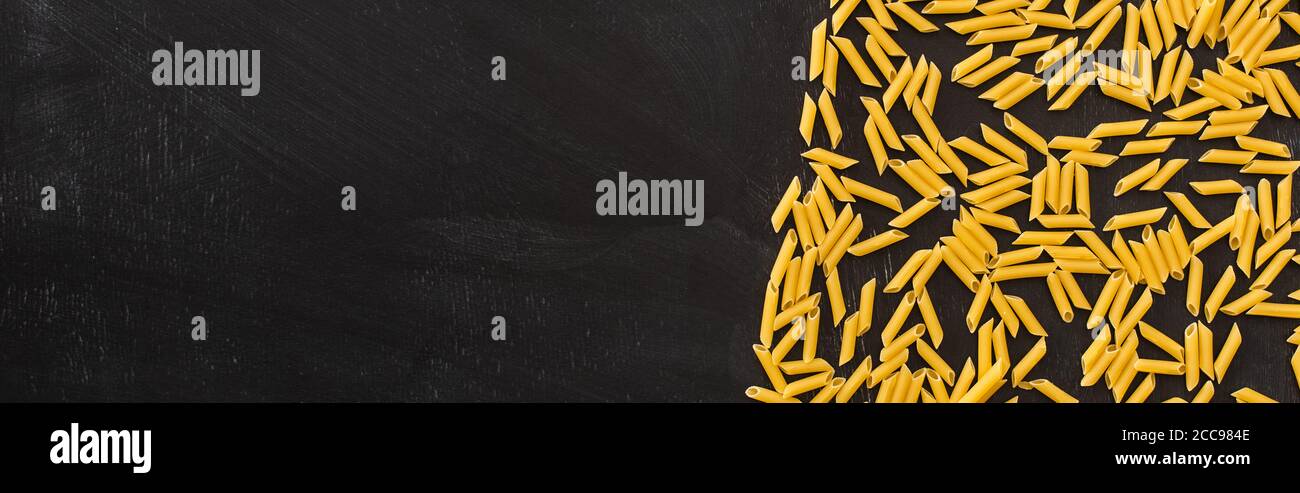 top view of raw penne pasta scattered on black background with copy ...