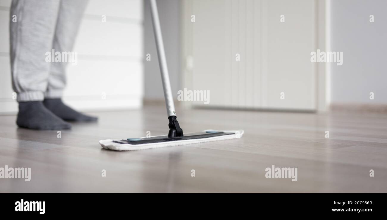 housekeeping concept - man cleaning wooden floor with mop in modern ...