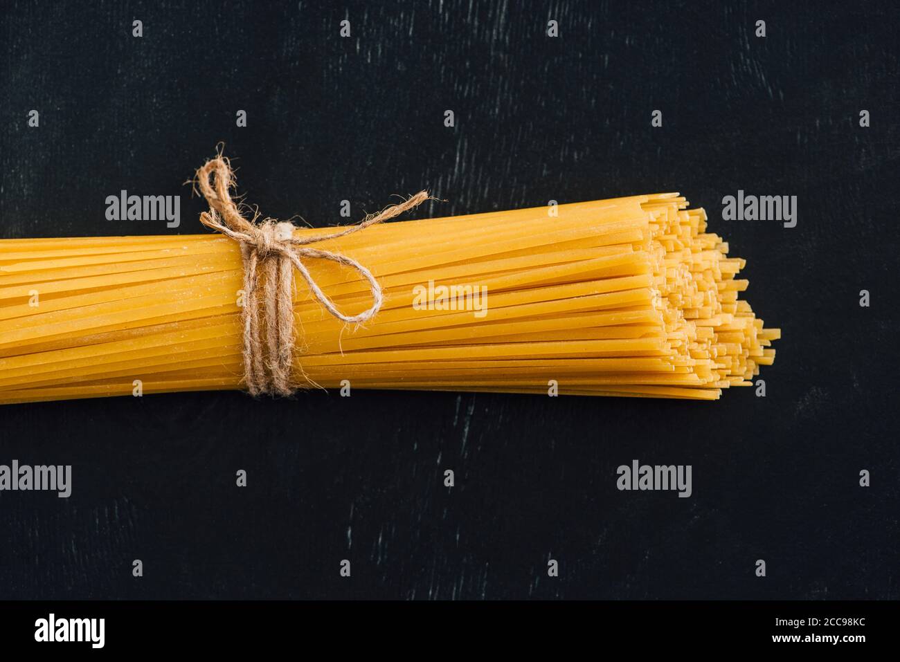top view of raw Italian spaghetti tied with string on black background ...
