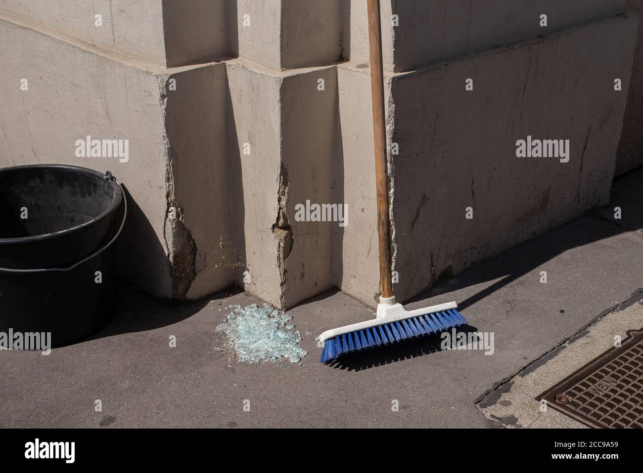A pile of broken shattered glass next to a blue broom and black bucket ...