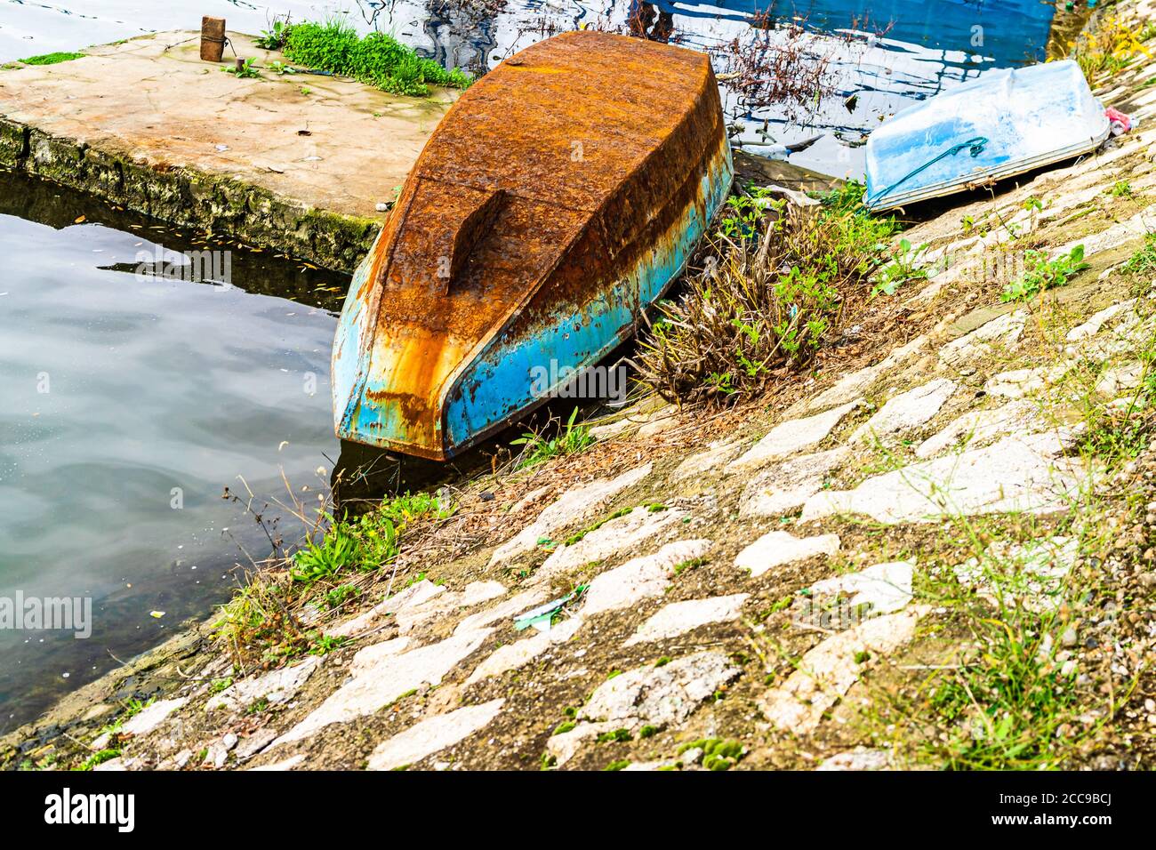 Old and rusty iron overturned boat on the shore, on the edge of a river ...