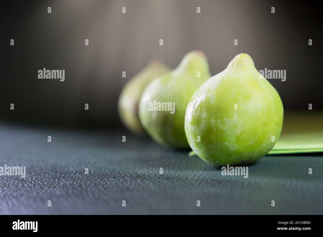 Close-up of fresh green italian figs with top light on a black ...