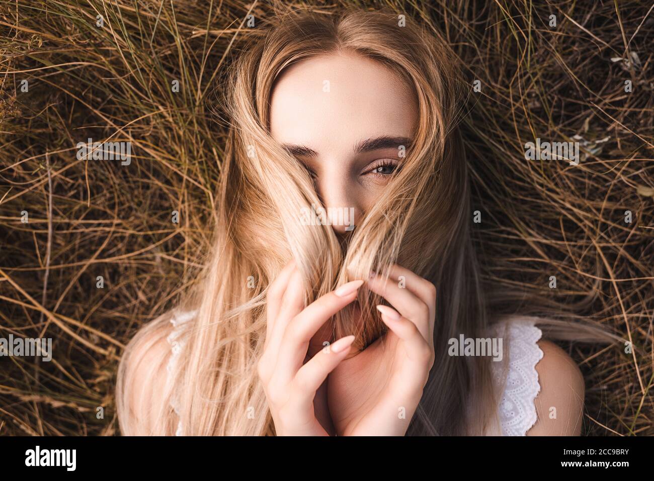 top view of young blonde woman obscuring face with hair while lying on ...
