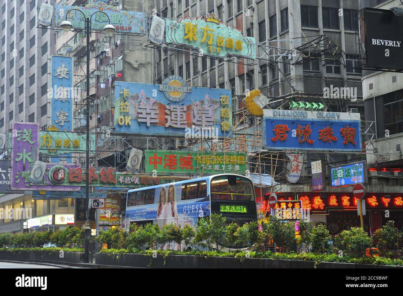 Double-decker bus passing under painted and neon-light signs. Kowloon ...