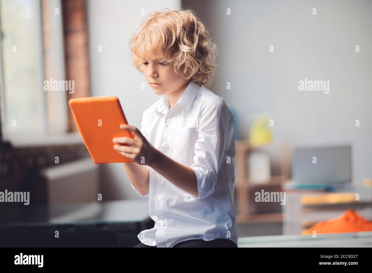 Cute blonde boy holding his tablet and typing a message Stock Photo - Alamy