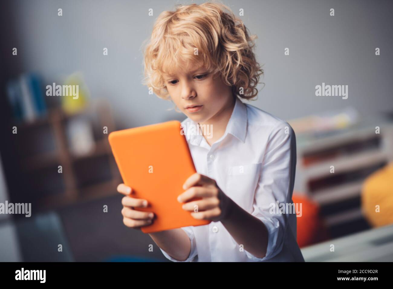 Cute blonde boy holding his tablet and reading something Stock Photo ...