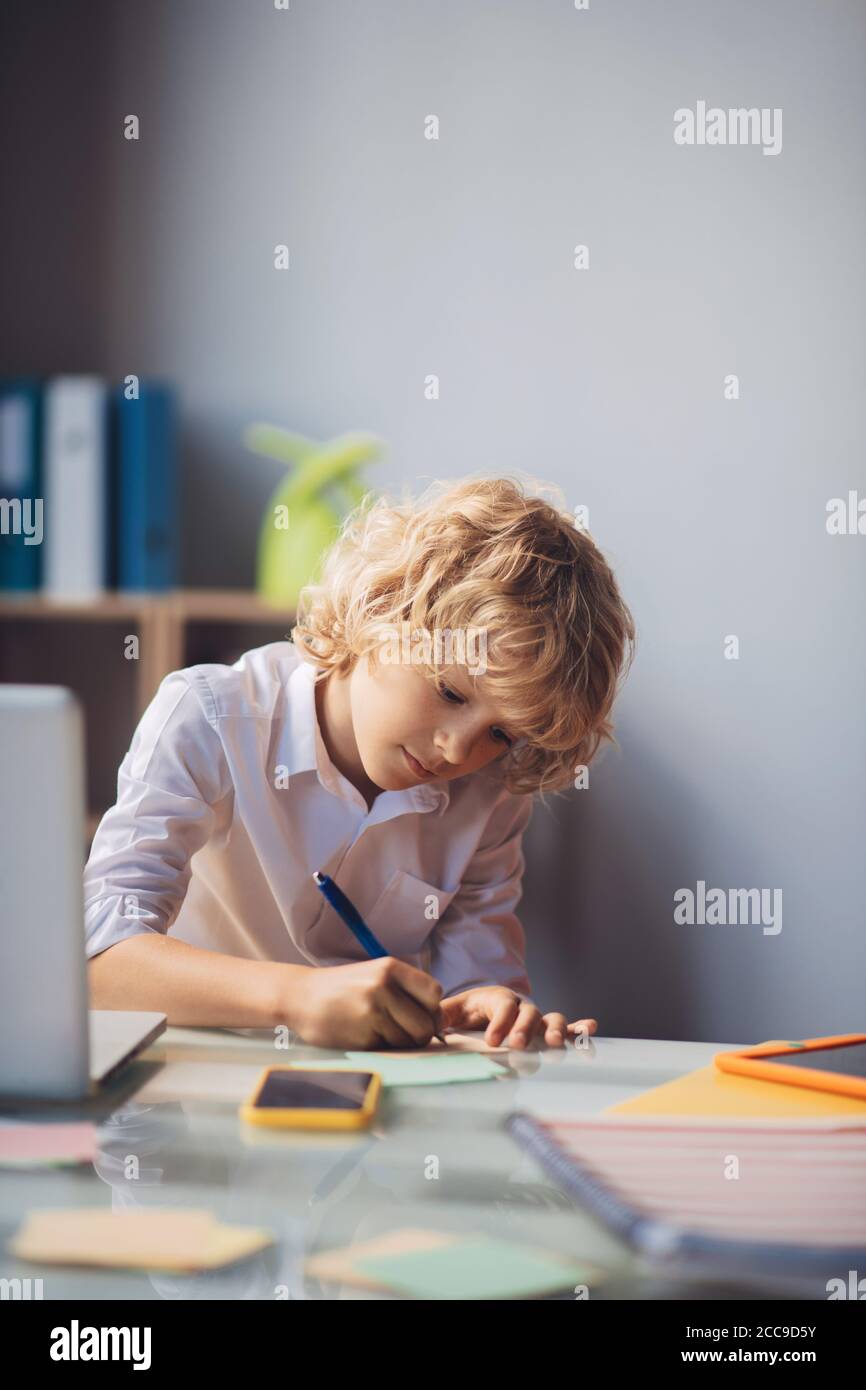 Cute blonde boy writing something and looking busy Stock Photo - Alamy