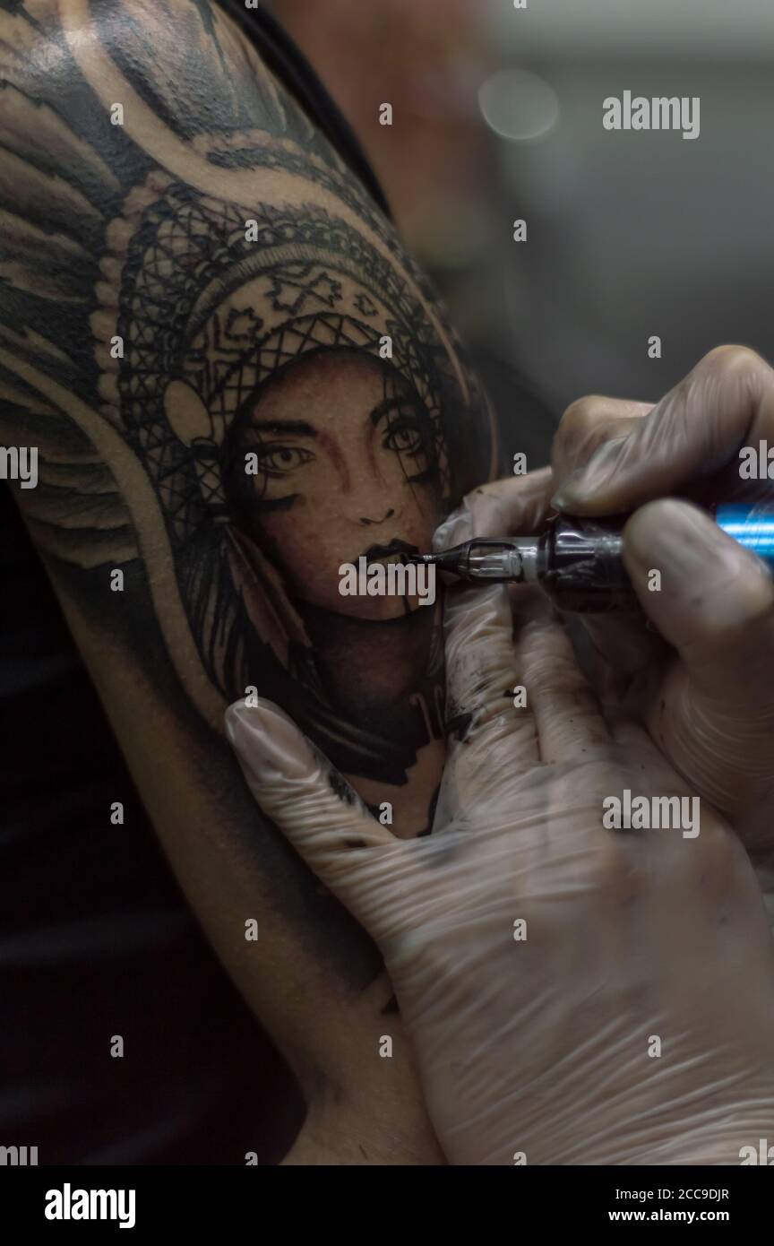 Vertical shot tattoo artist holding a tattoo machine tattooing a person ...