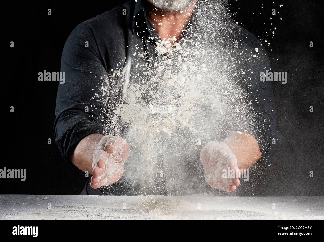 chef in black uniform sprinkles white wheat flour in different ...