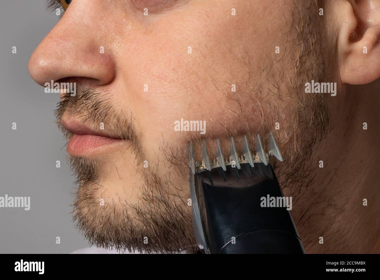 A man shaves his beard with a trimmer razor. Modeling beard, masculine ...