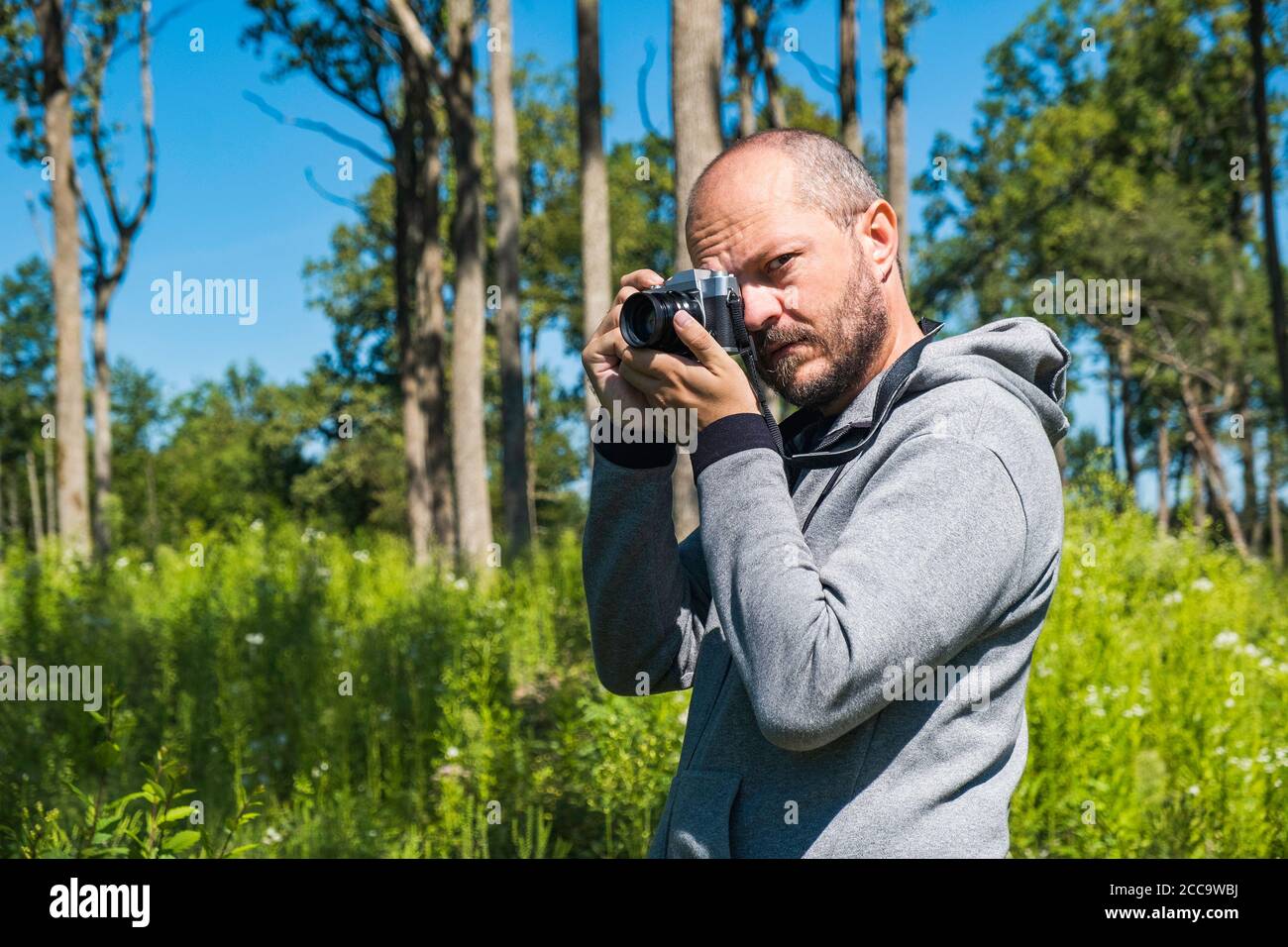 Adult man holding mirror less camera, shooting photos in a forest in ...