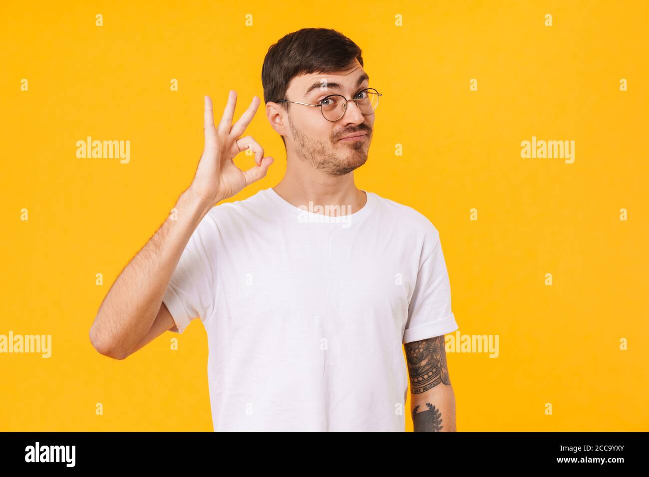 Photo of amusing young man in eyeglasses making ok sign and looking at ...