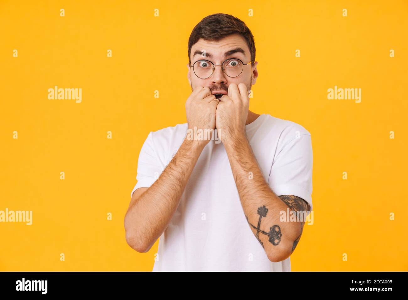 Photo of scared young man in eyeglasses looking at camera and covering ...
