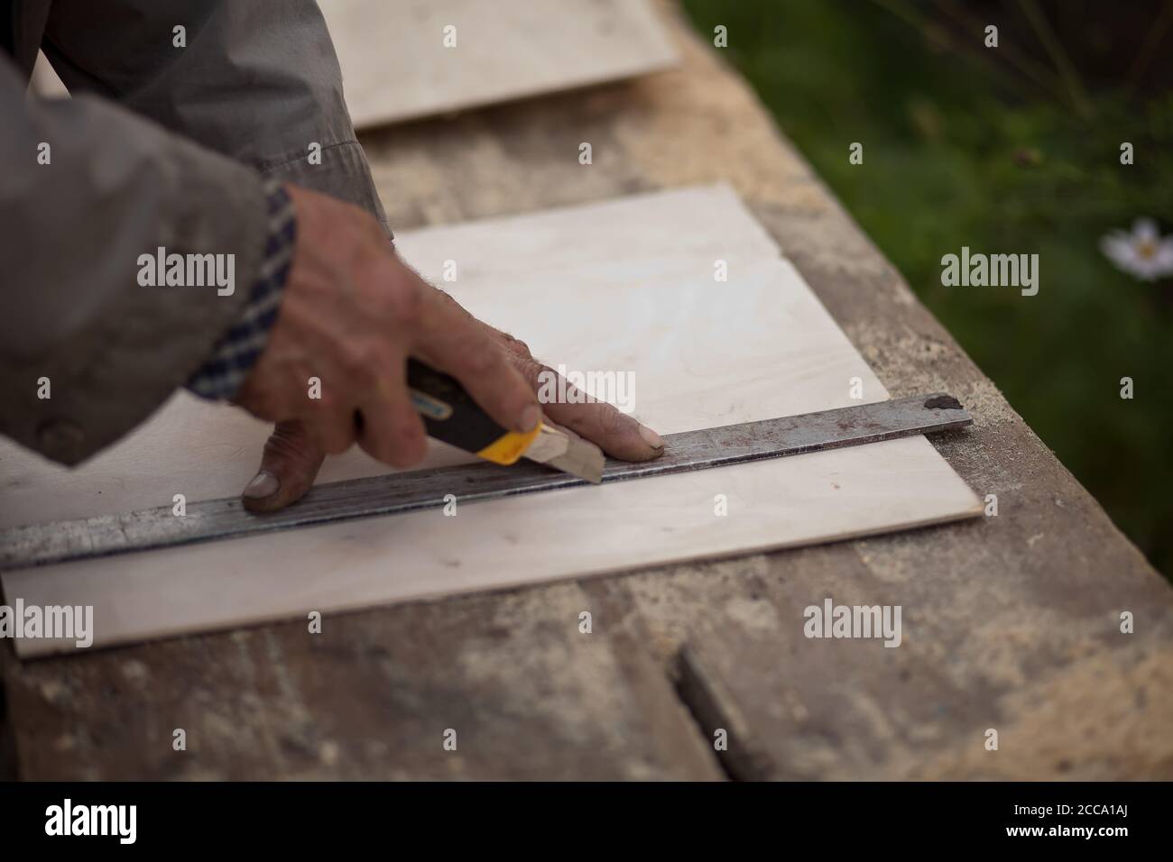 Senior elderly carpenter using a straightedge to draw a line on a board ...