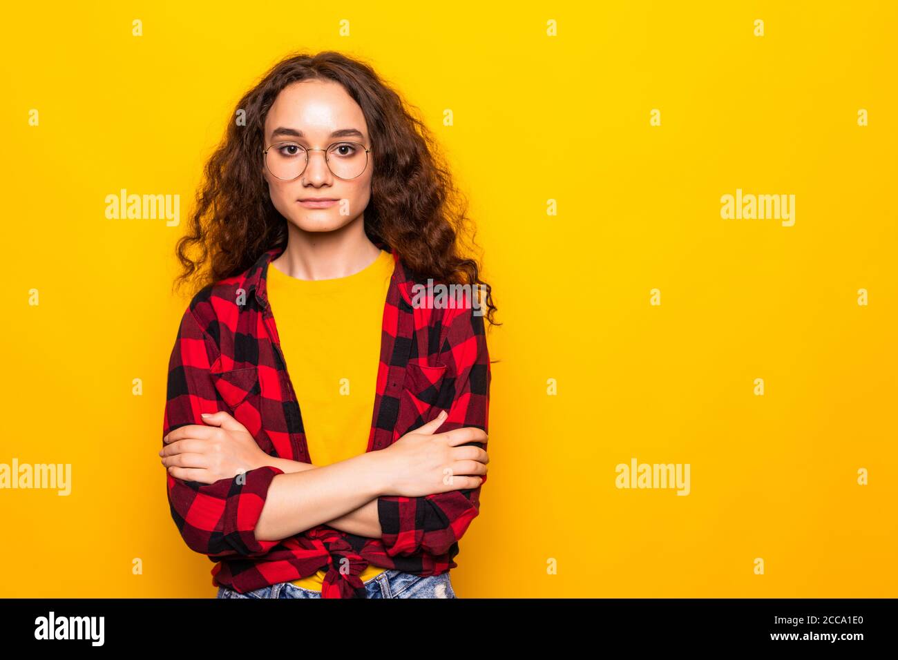 Portrait of a young woman standing with arms folded over yellow ...