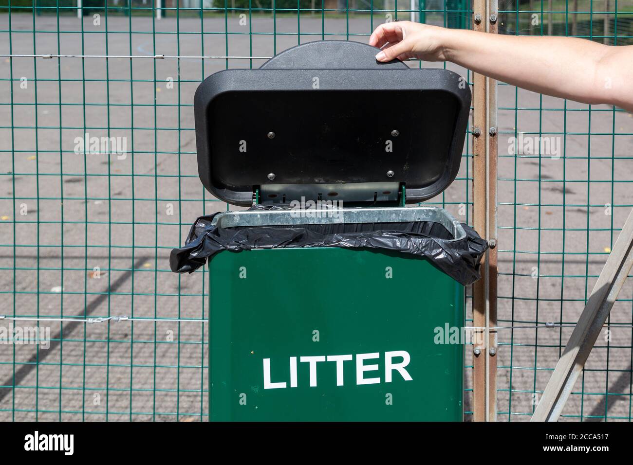 A hand lifting the lid of a green litter bin in the park Stock Photo ...