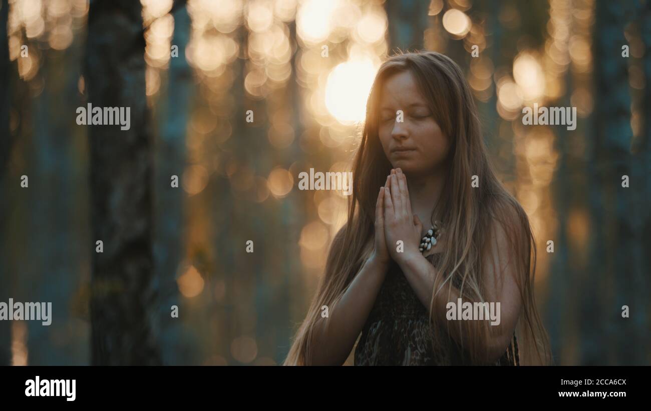 young woman praying with closed eyes in nature during the sunset ...