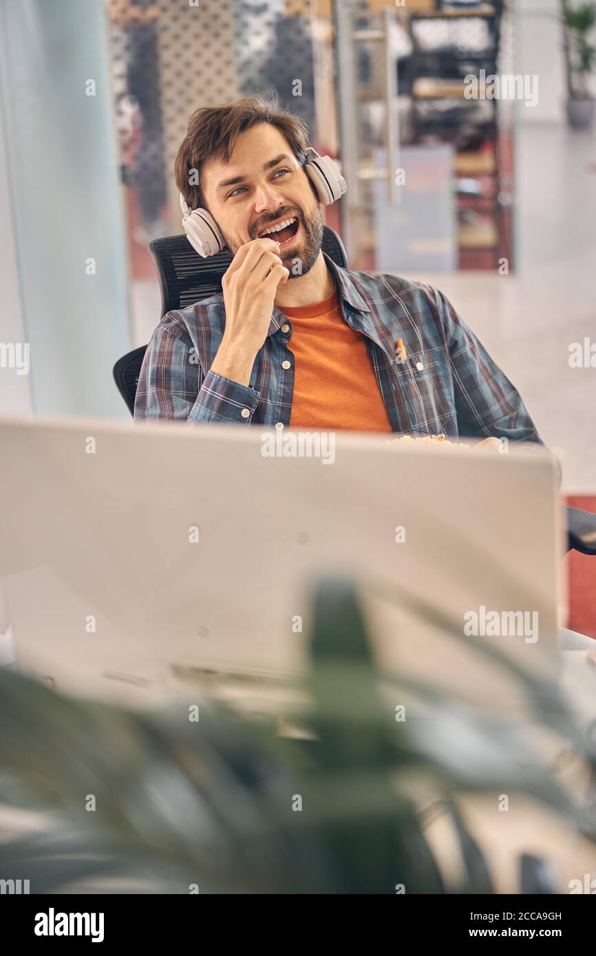 Joyful young man eating popcorn at work Stock Photo - Alamy