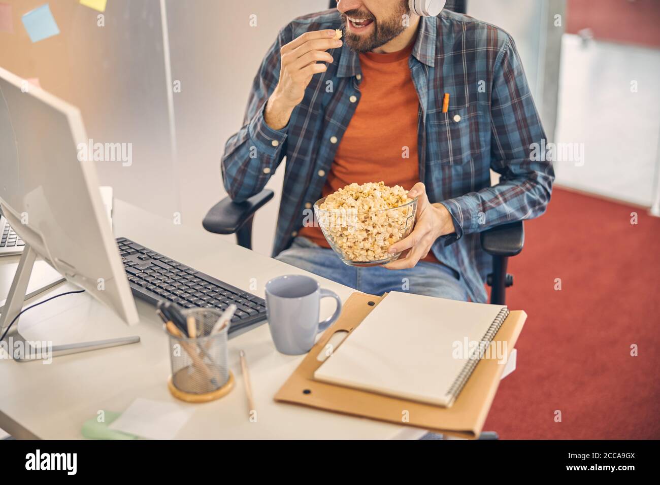 Bearded young man eating popcorn at work Stock Photo - Alamy