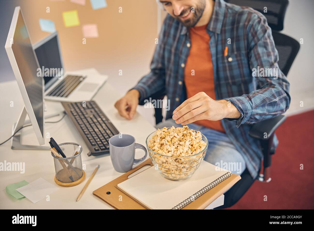 Cheerful young man eating popcorn at work Stock Photo - Alamy