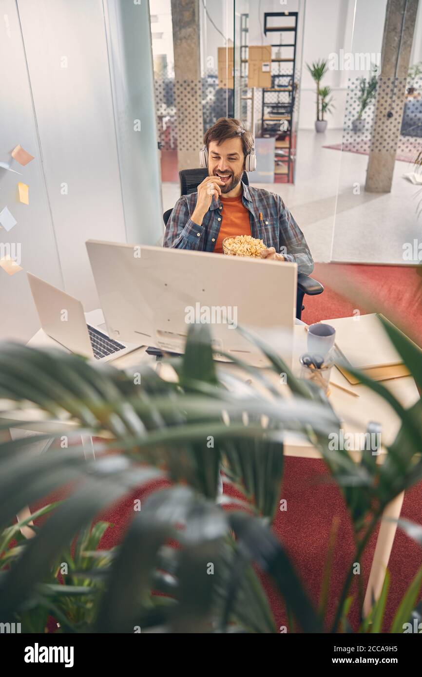 Cheerful young man eating popcorn at work Stock Photo - Alamy