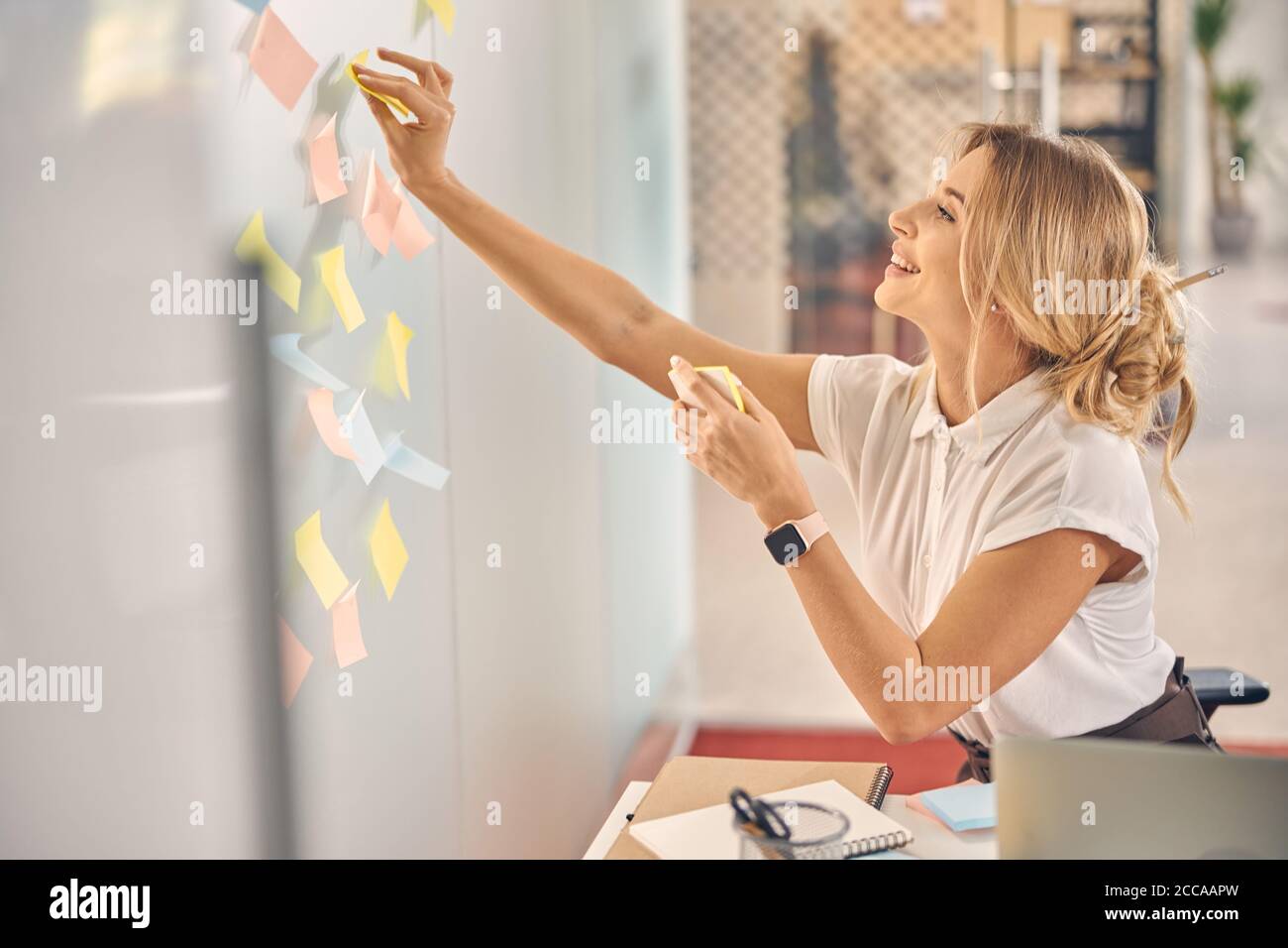Beautiful young woman putting sticky note on the wall Stock Photo - Alamy