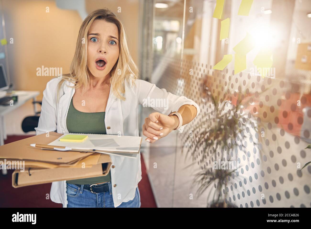 Shocked young woman with papers standing in office Stock Photo - Alamy