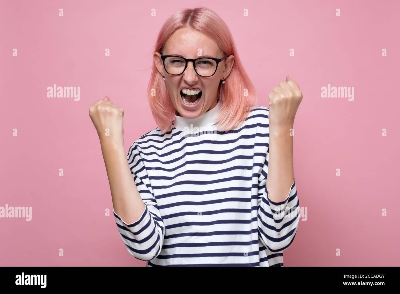 woman with pink dyed hair raising arms, clenching fists, exclaiming ...