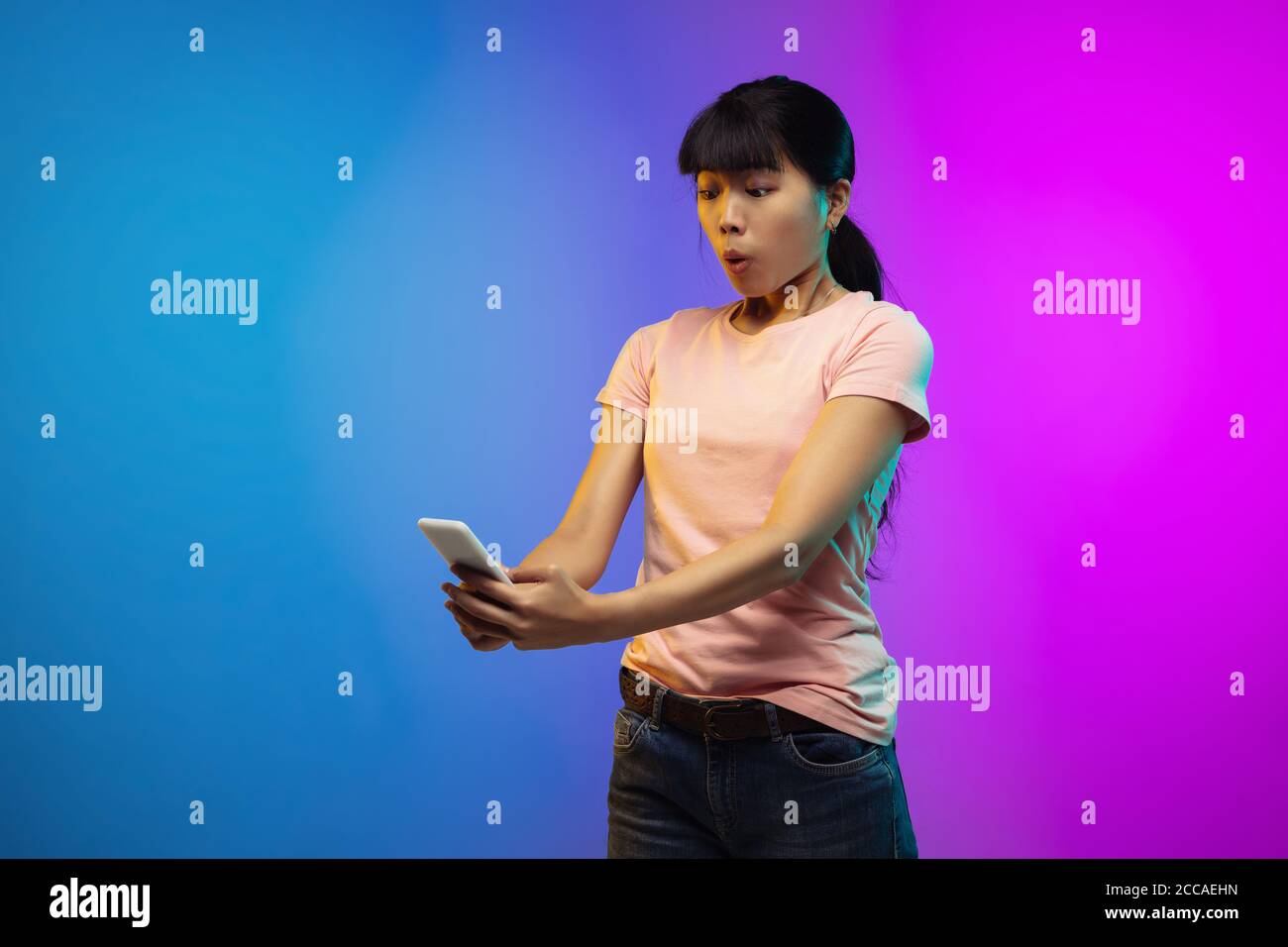 Scrolling phone, shocked. Asian young woman's portrait on gradient ...