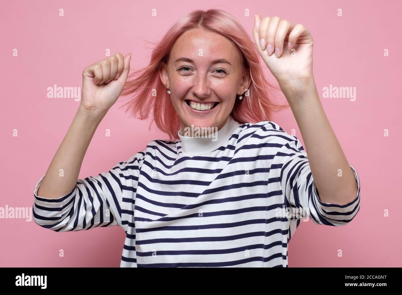 woman with pink dyed hair raising arms, clenching fists, exclaiming ...