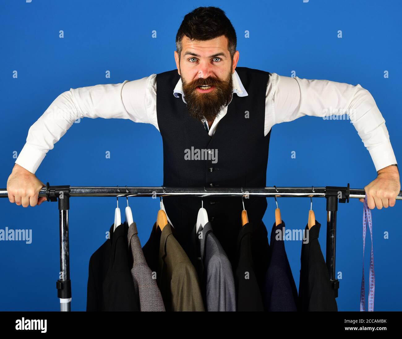 Tailor with mad face near custom jackets on blue background. Designer ...