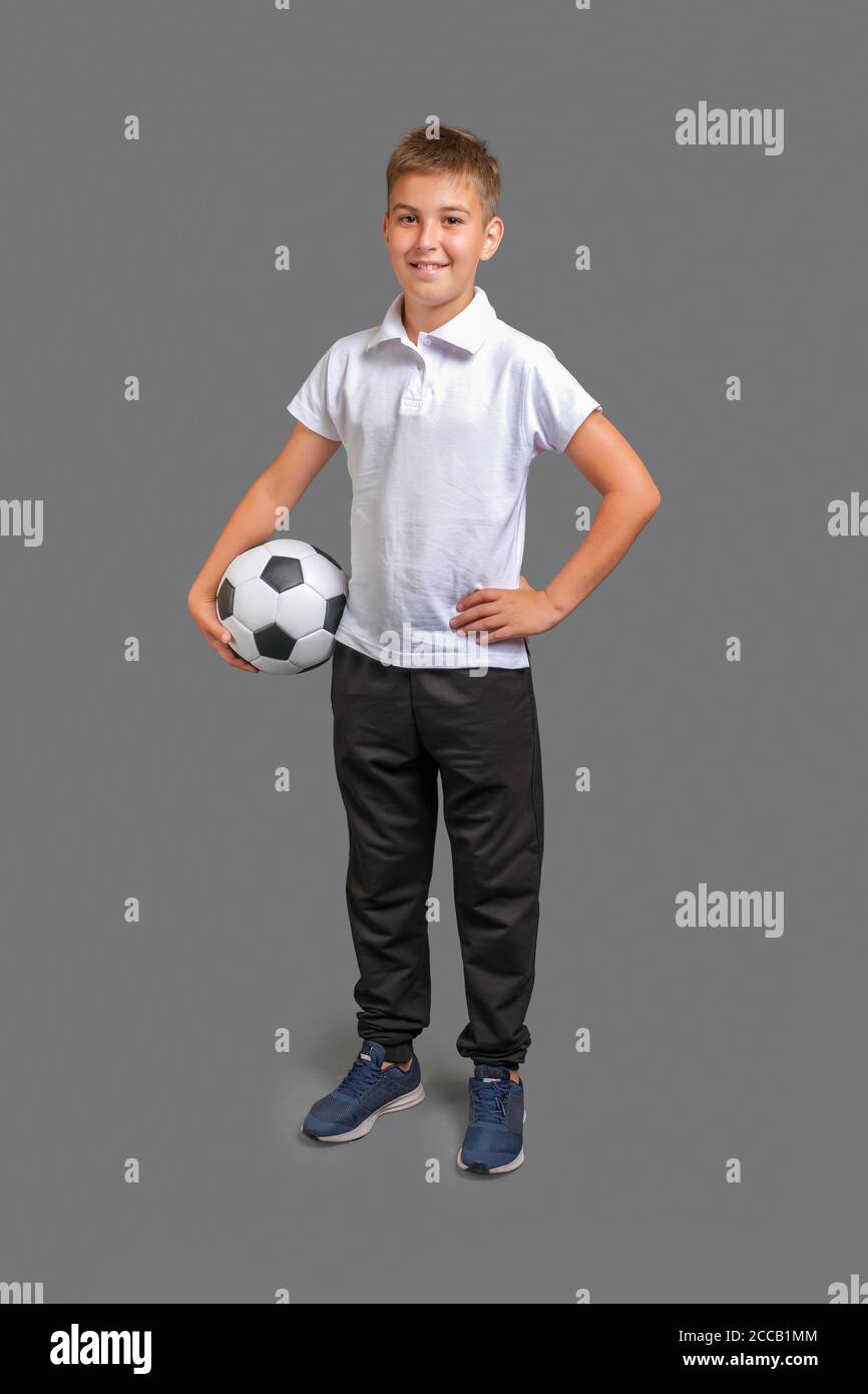 Kid holds in hand a classic soccer ball and smiling isolated on gray ...