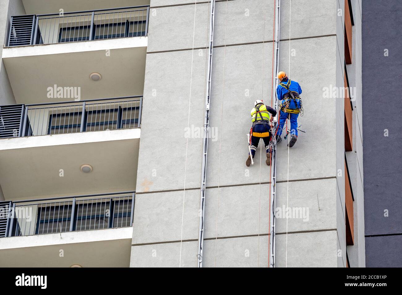 Two workers hang on the building and doing electrical installations in ...