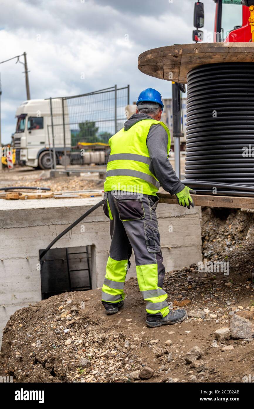 Worker unrolls black wire electrical cable with wooden coil. Laying the ...