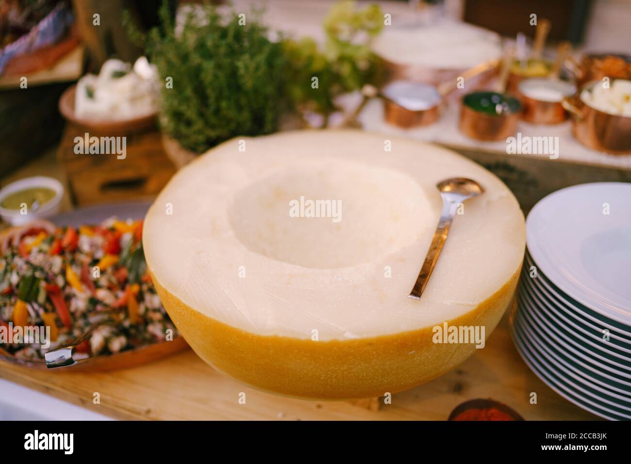 Half a cheese ball on a wooden table with a spoon, plates and salad on ...