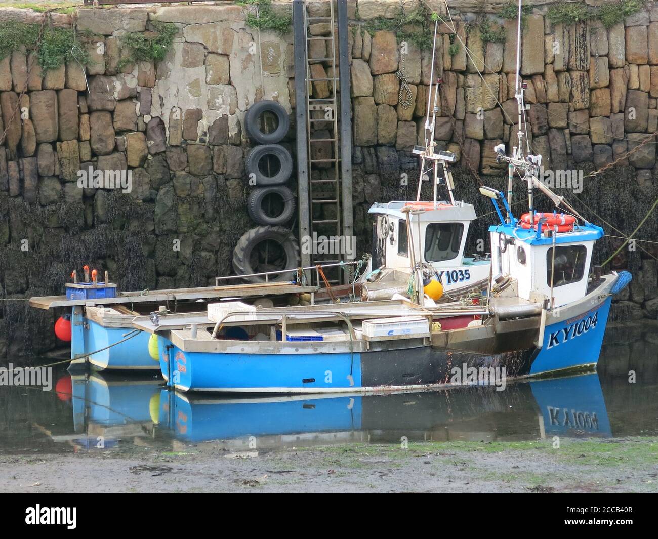 Fishing boats moored by the harbour wall at Crail, a traditional way of ...