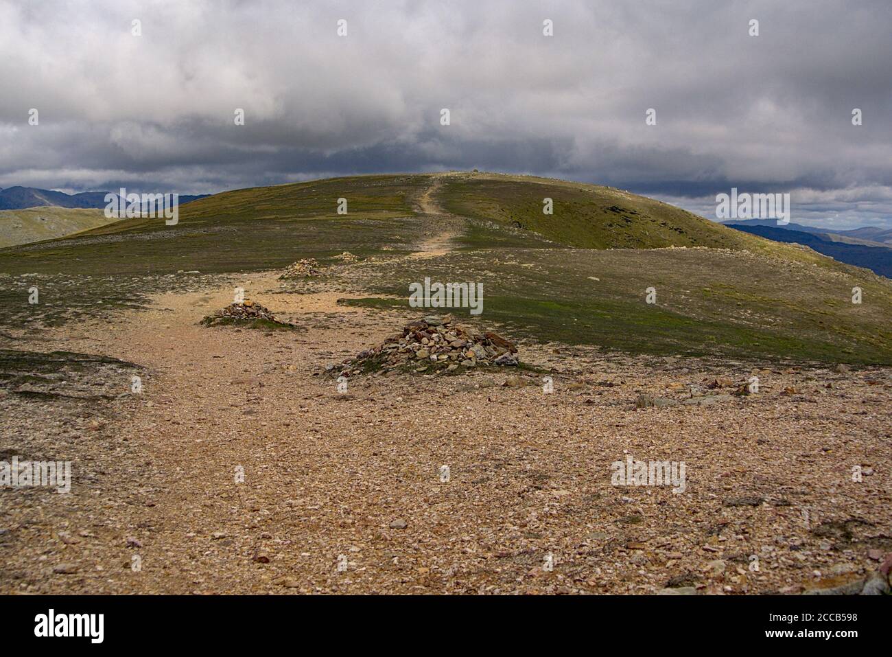 Pebble area and path heading over large hill with surrounding mountains ...