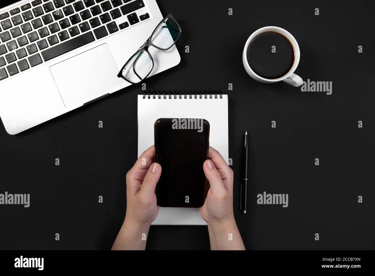 hands hold phone over notepad next to computer. black background Stock ...