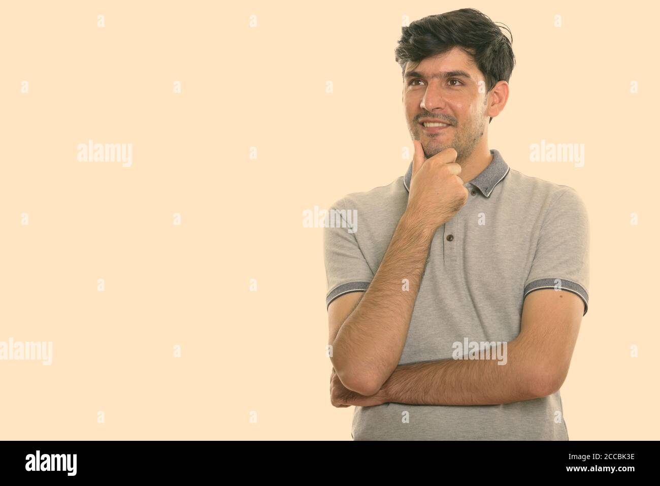 Studio shot of young happy Persian man smiling and thinking while ...