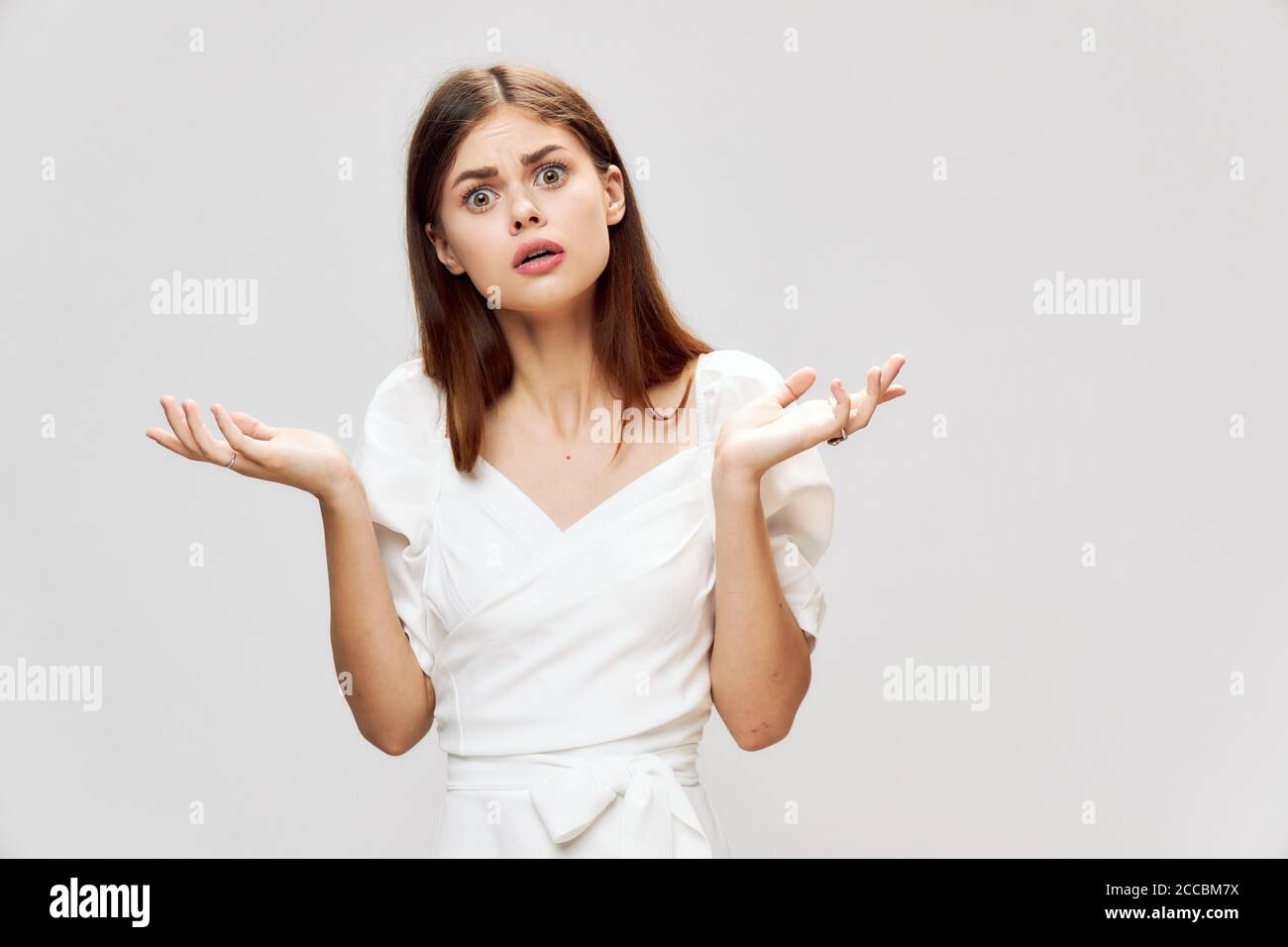 Woman with surprised facial expression shrugs white dress emotions gray ...