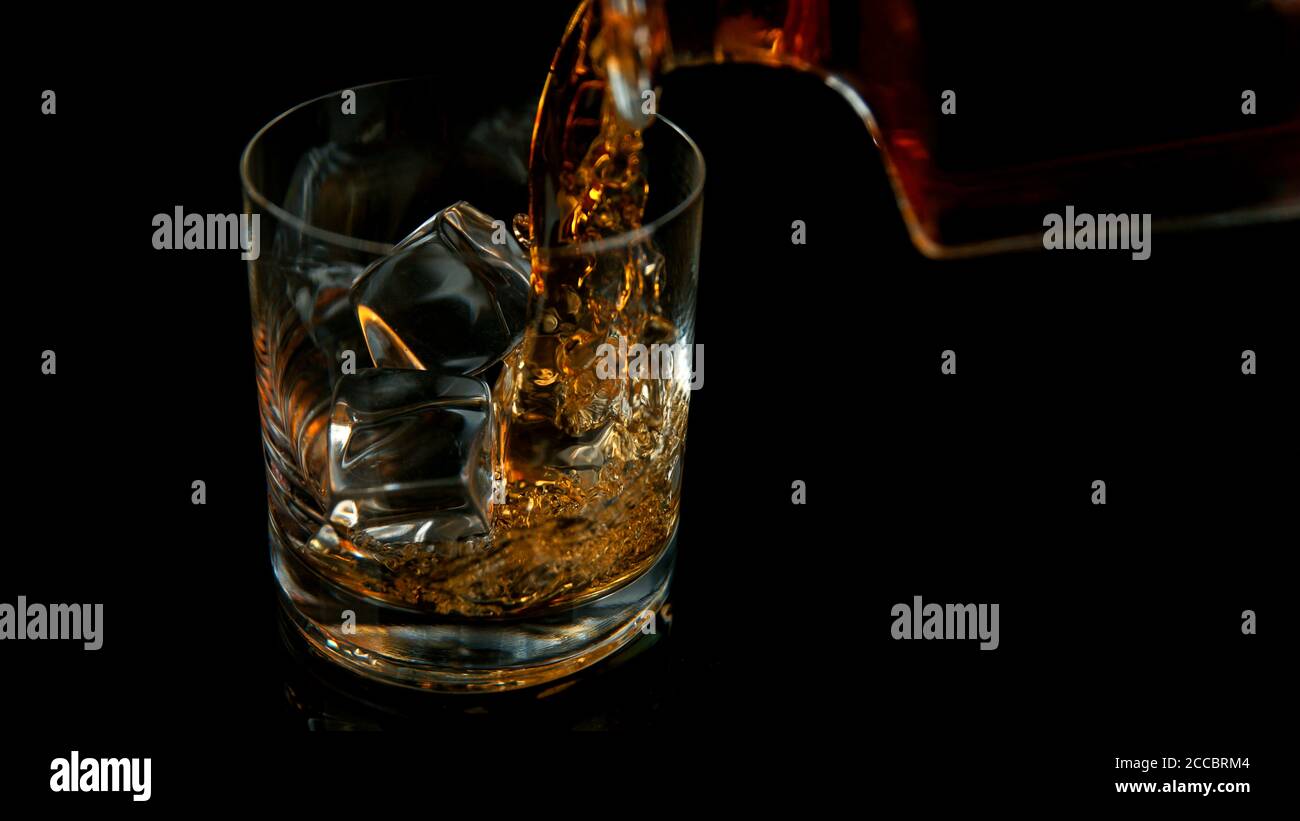Detail of pouring whiskey into glass on black background Stock Photo - Alamy