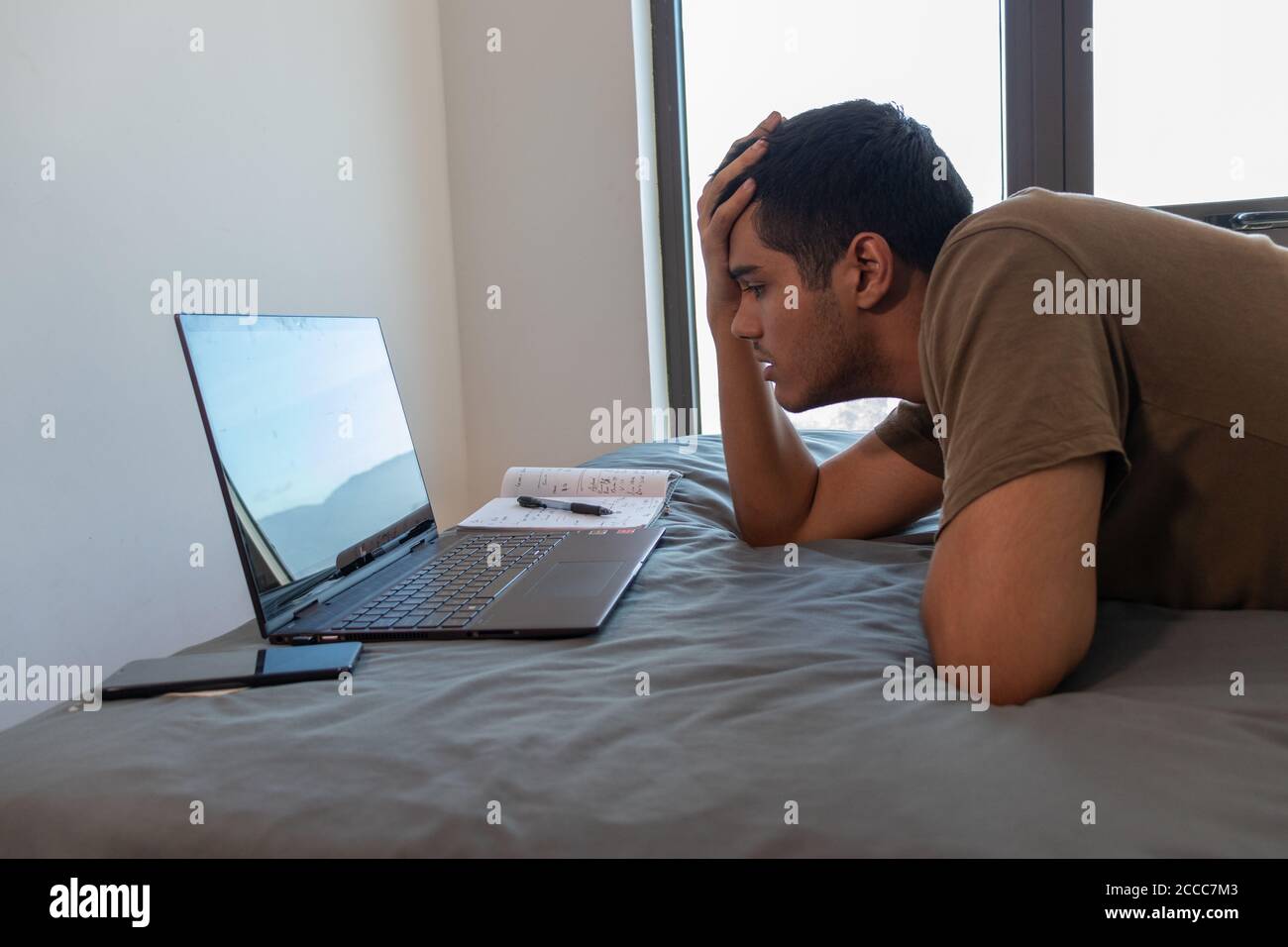 Male touching his forehead with a stressed look while studying a ...