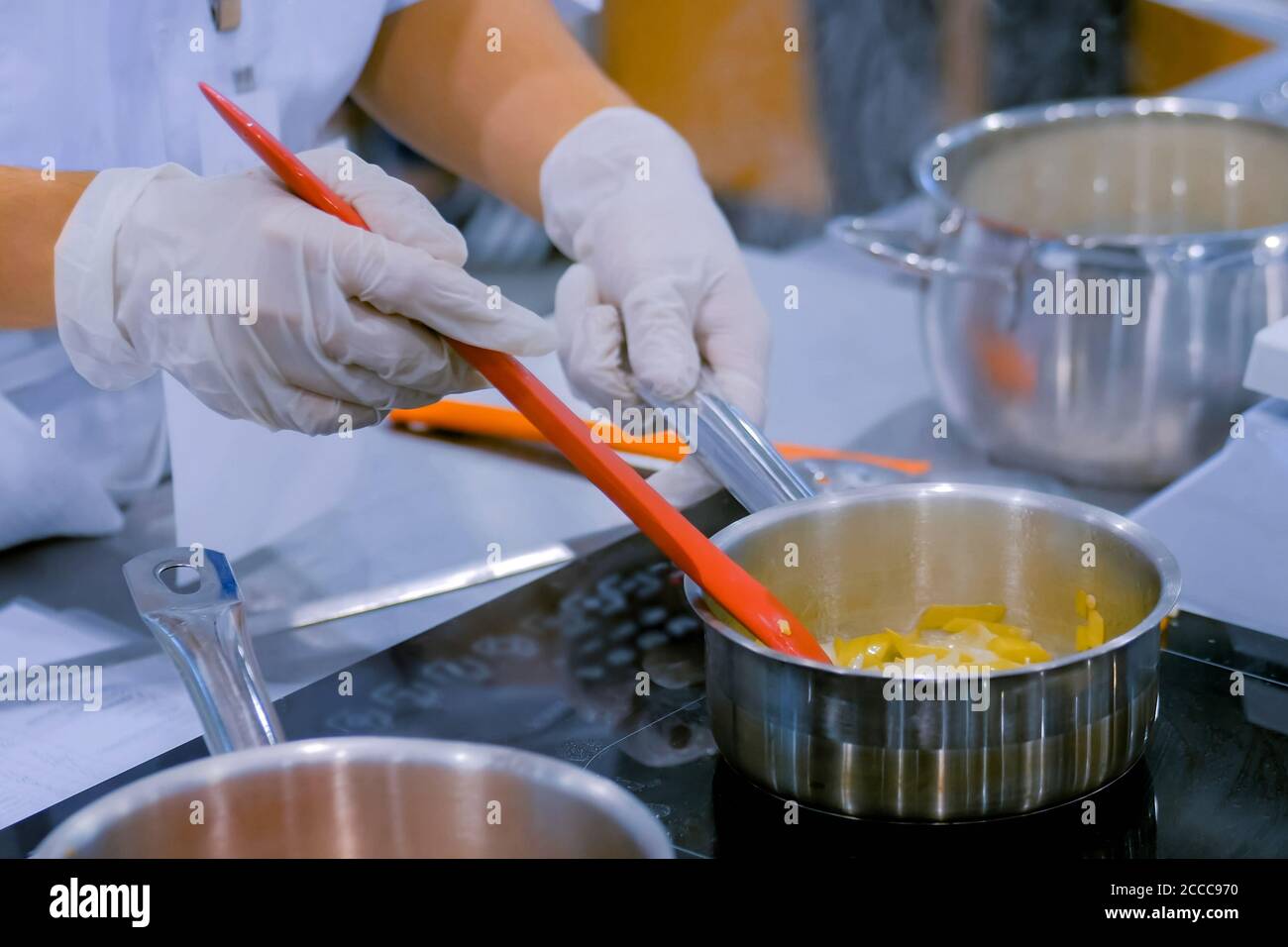 Chef hand stirring vegetables with spoon in pot on electric stove at ...