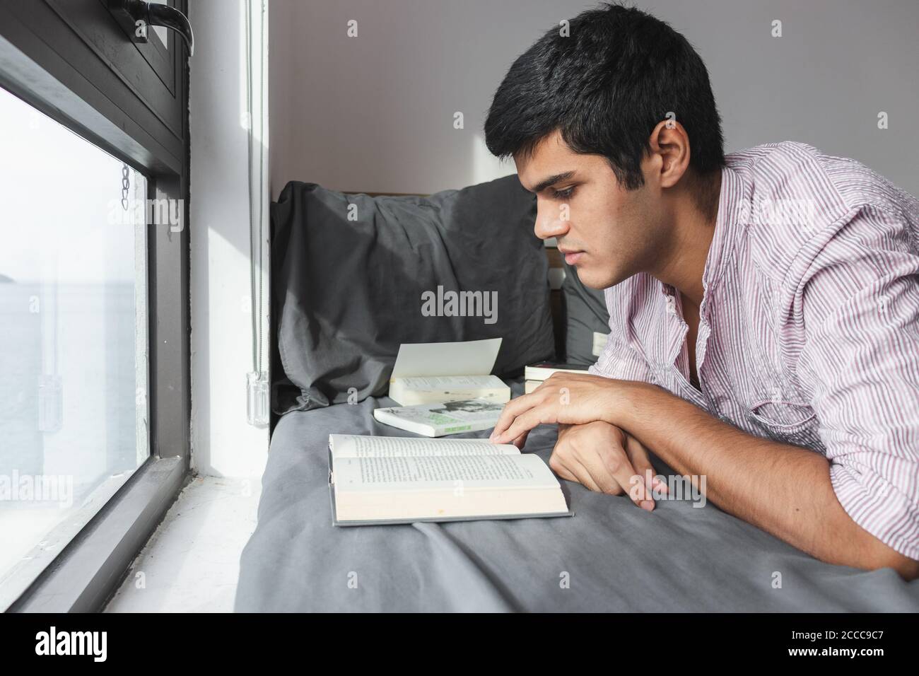 Indian male reading a book on the bed by a window with a nice view ...