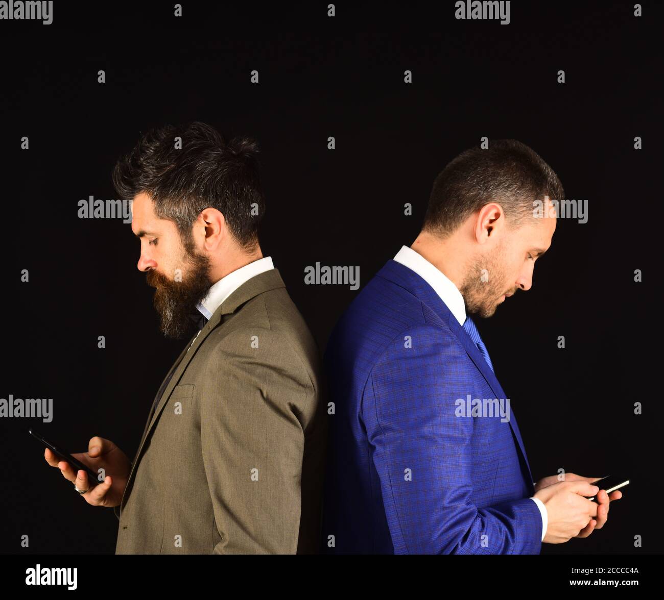 Machos in classic suits text on mobile phone. Businessmen with ...